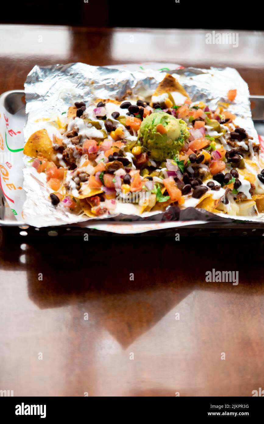 A vertical shot of Mexican nachos with sour cream, guacamole, and ...