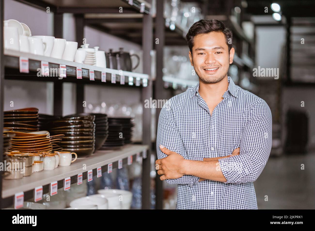 Handsome asian man standing with hands crossed standing beside shelf ...
