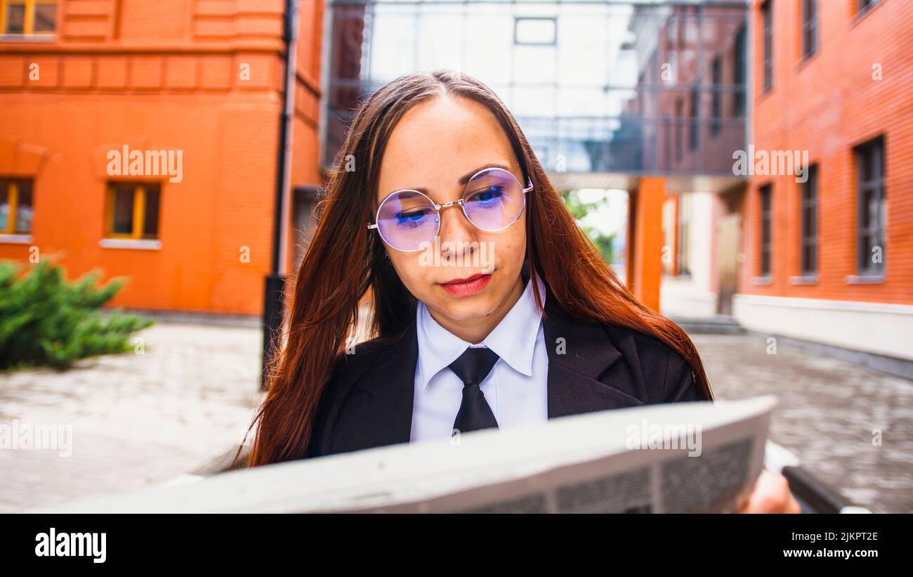 Thoughtful young woman reading newspaper on street. Confused young ...