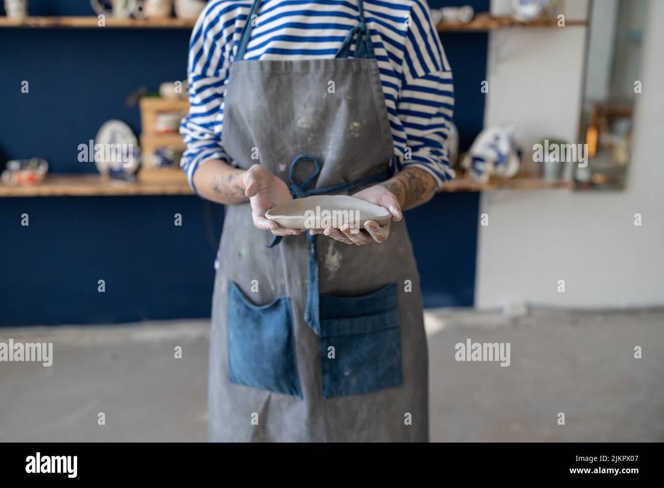 Woman ceramic artist wearing dirty apron holding unfinished unbaked ...