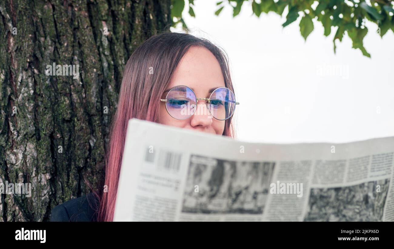 Concentrated elegant lady reading newspaper in park. Focused young ...