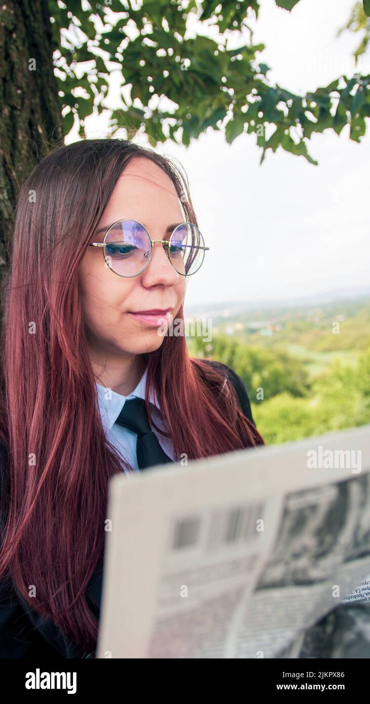 Concentrated elegant lady reading newspaper in park. Focused young ...