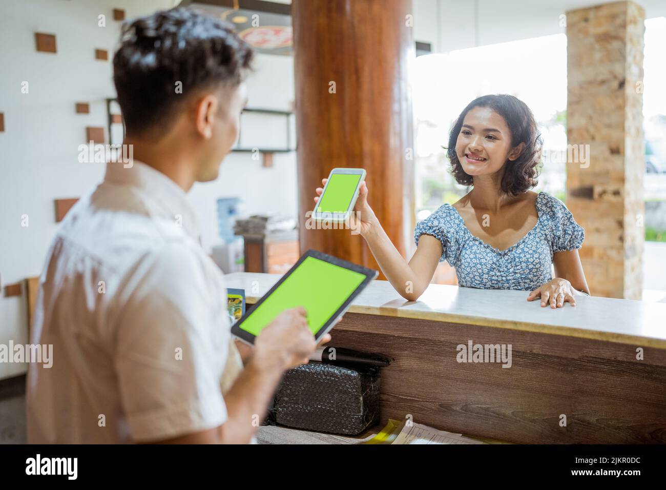 Female guest showing smartphone at receptionist holding tablet Stock ...