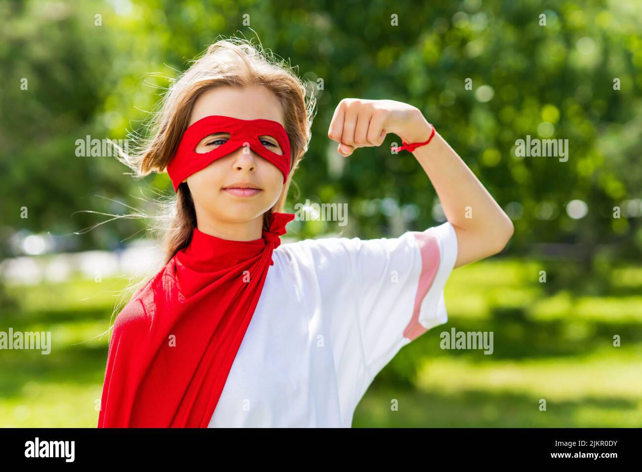 Funny teenager girl playing power super hero over green park background ...