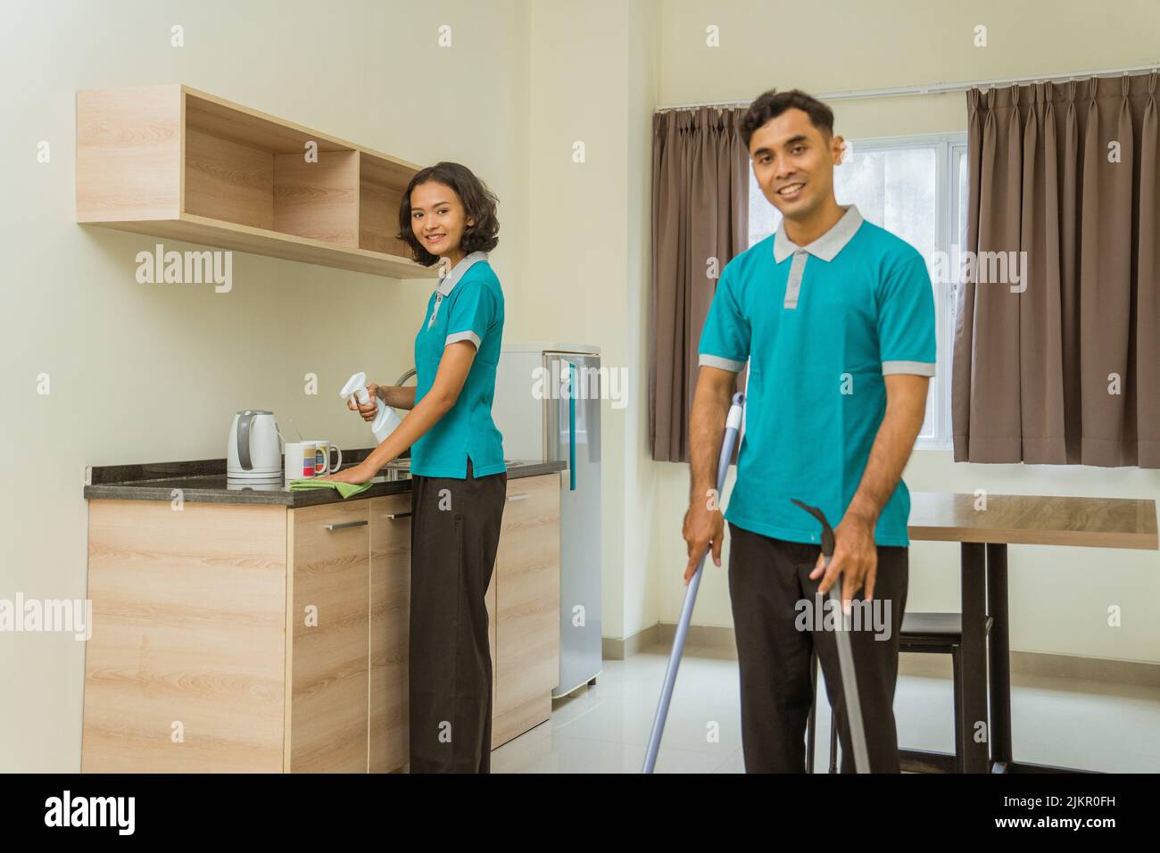 male and female janitor in turquoise uniform sweeping and cleaning ...