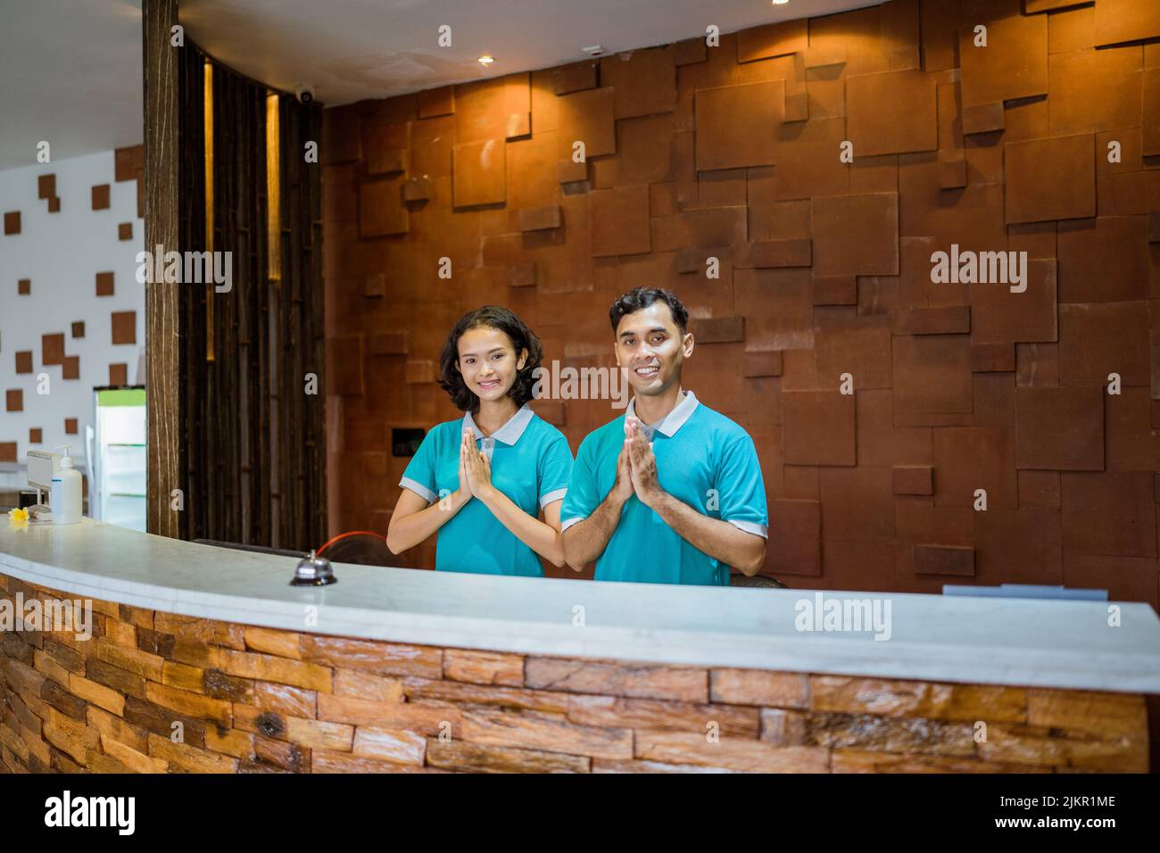 two employees wearing uniforms smiling with hand gestures greeting ...