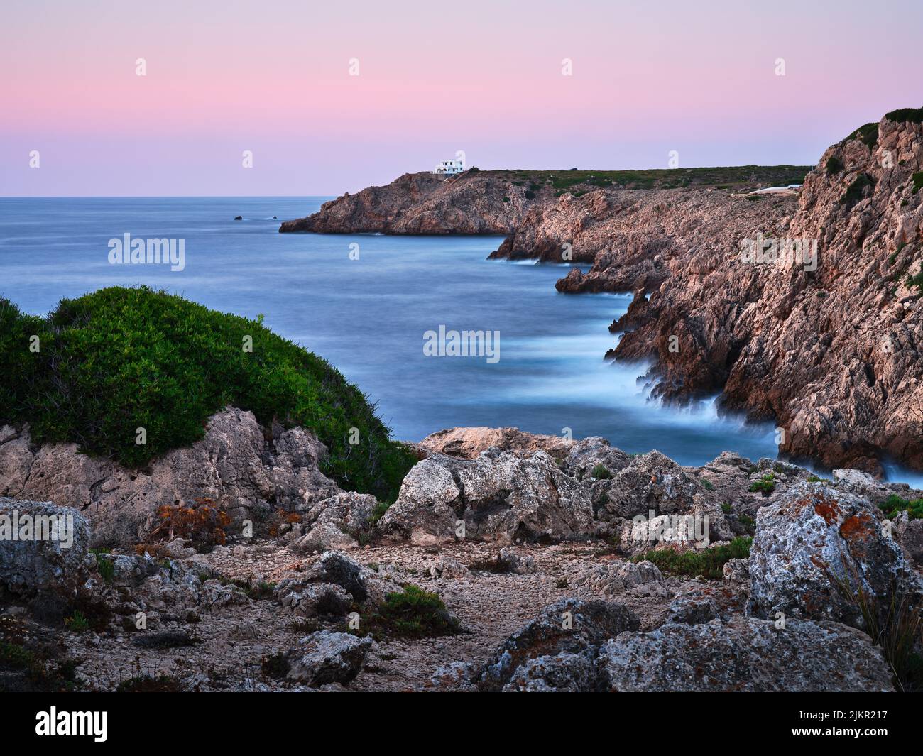 The rocky coast of Menorca island and the house at the end of the cliff ...