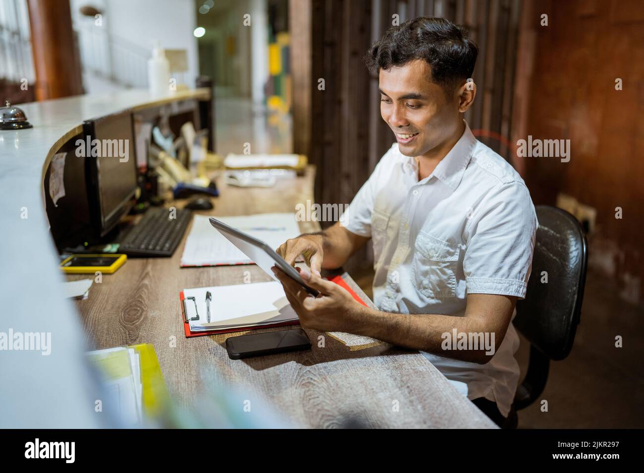receptionist using digital tablet while sitting at hotel reception desk ...