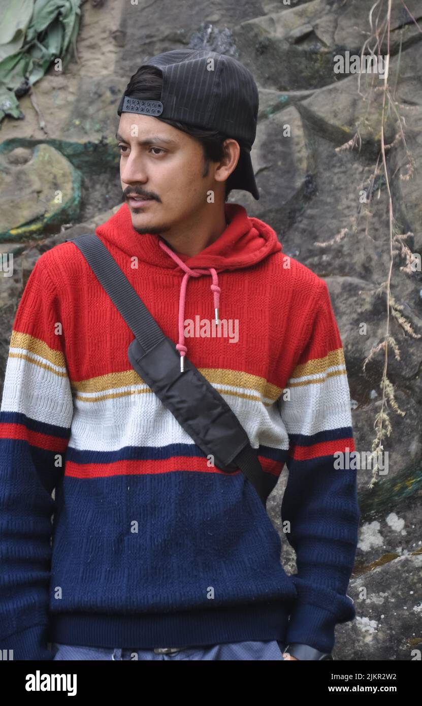Front view of a young guy with wearing cap backwards, looking sideways while posing with hands ...