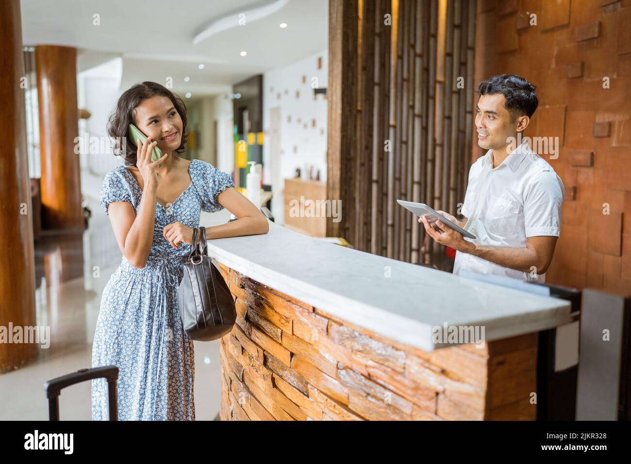 Asian female guest calling using smartphone while receptionist using ...