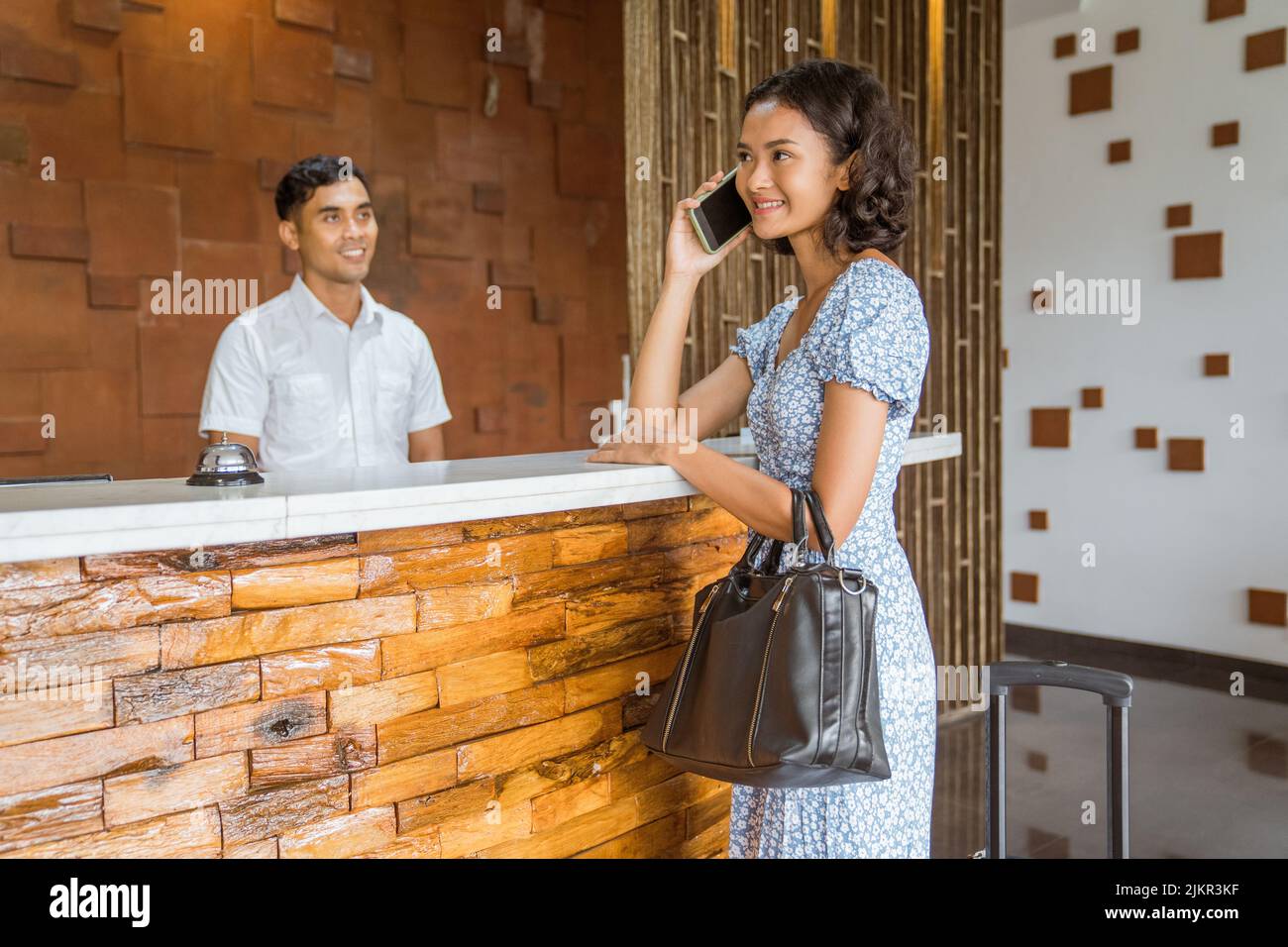 Female guest calling with smartphone at reception in hotel lobby Stock ...
