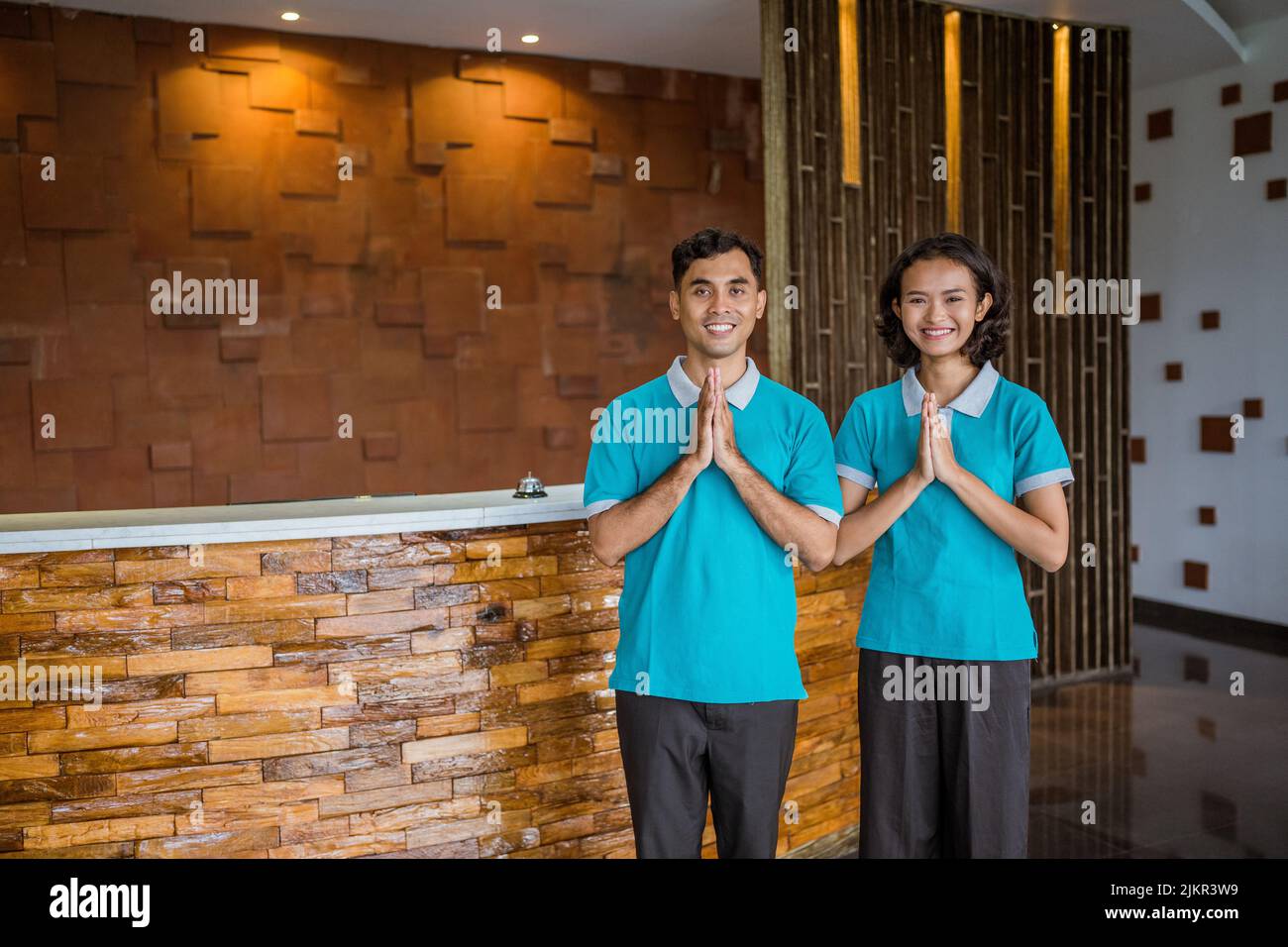 two receptionists wearing turquoise uniforms smiling with welcome hands ...