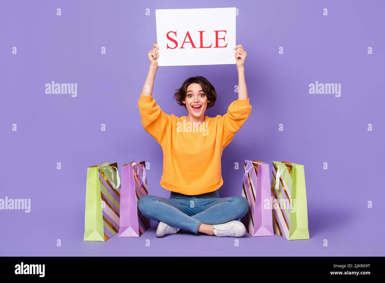 Portrait of attractive cheerful funny girl holding sale board sitting ...