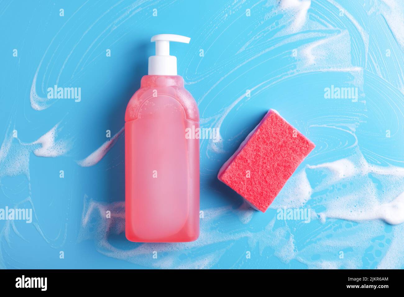 Dishwashing liquid and red sponge on foaming wet blue background ...
