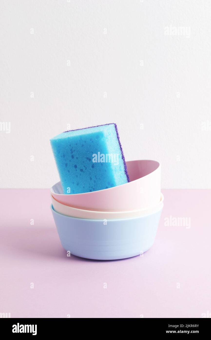 Blue cleaning sponge in colorful bowls on pink and white background ...