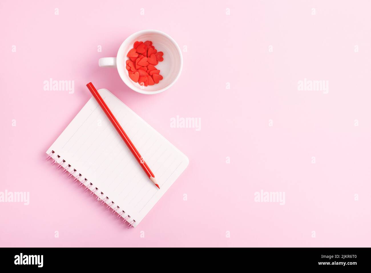 Romantic pink background with white notebook page, red pencil and ...