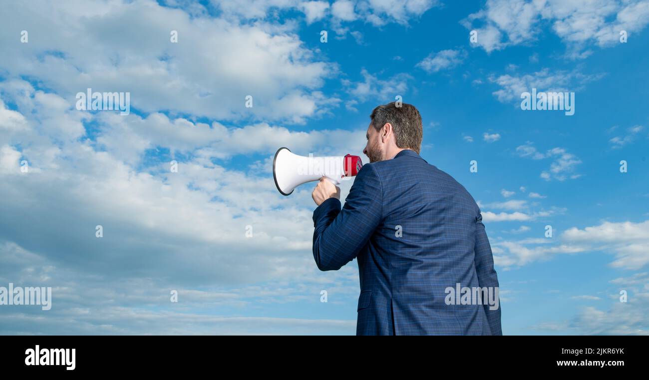 back view of businessman shout in loudspeaker on sky background. copy ...