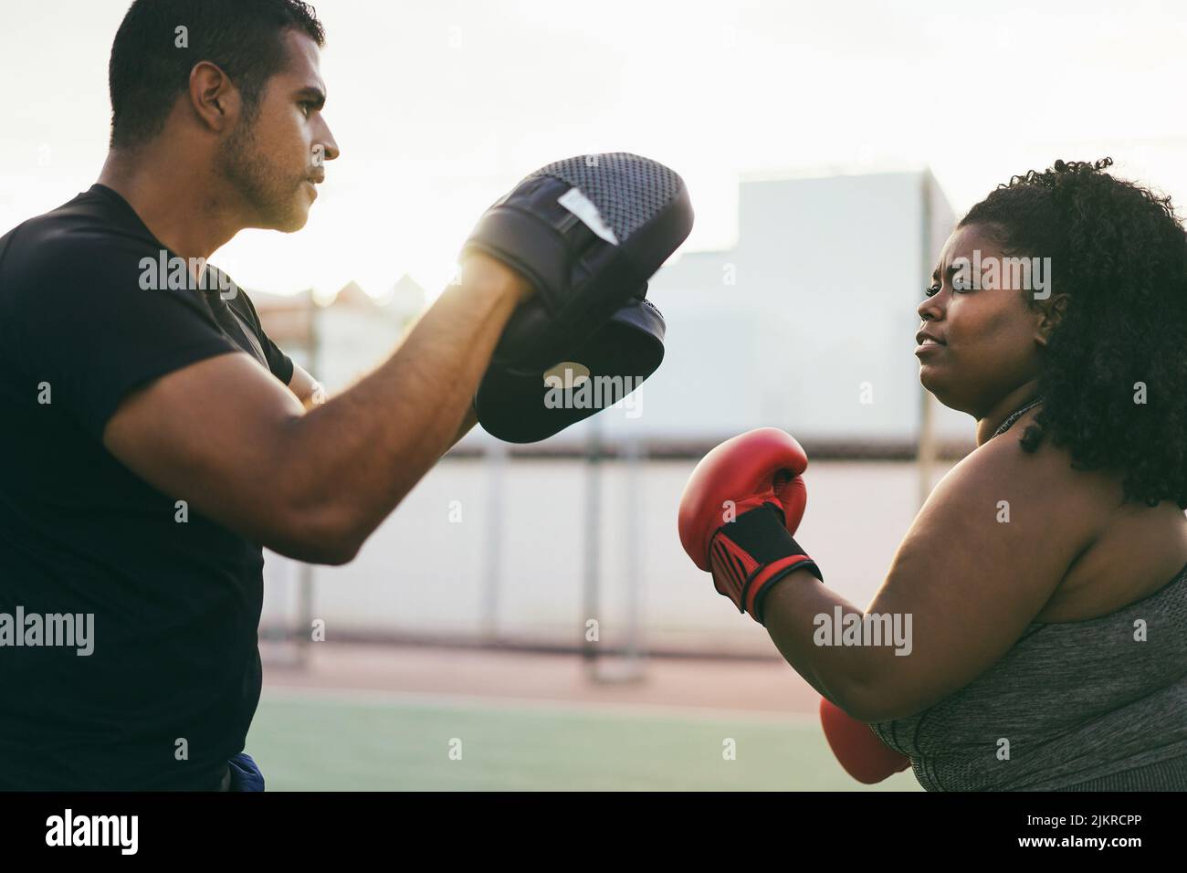 African curvy woman and personal trainer doing boxing workout session ...