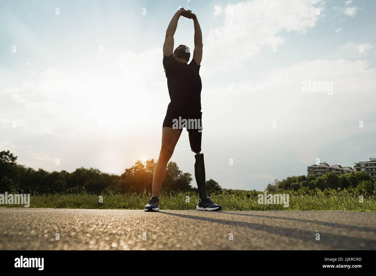 Young fit man with prosthetic leg doing stretching day routine outdoor ...