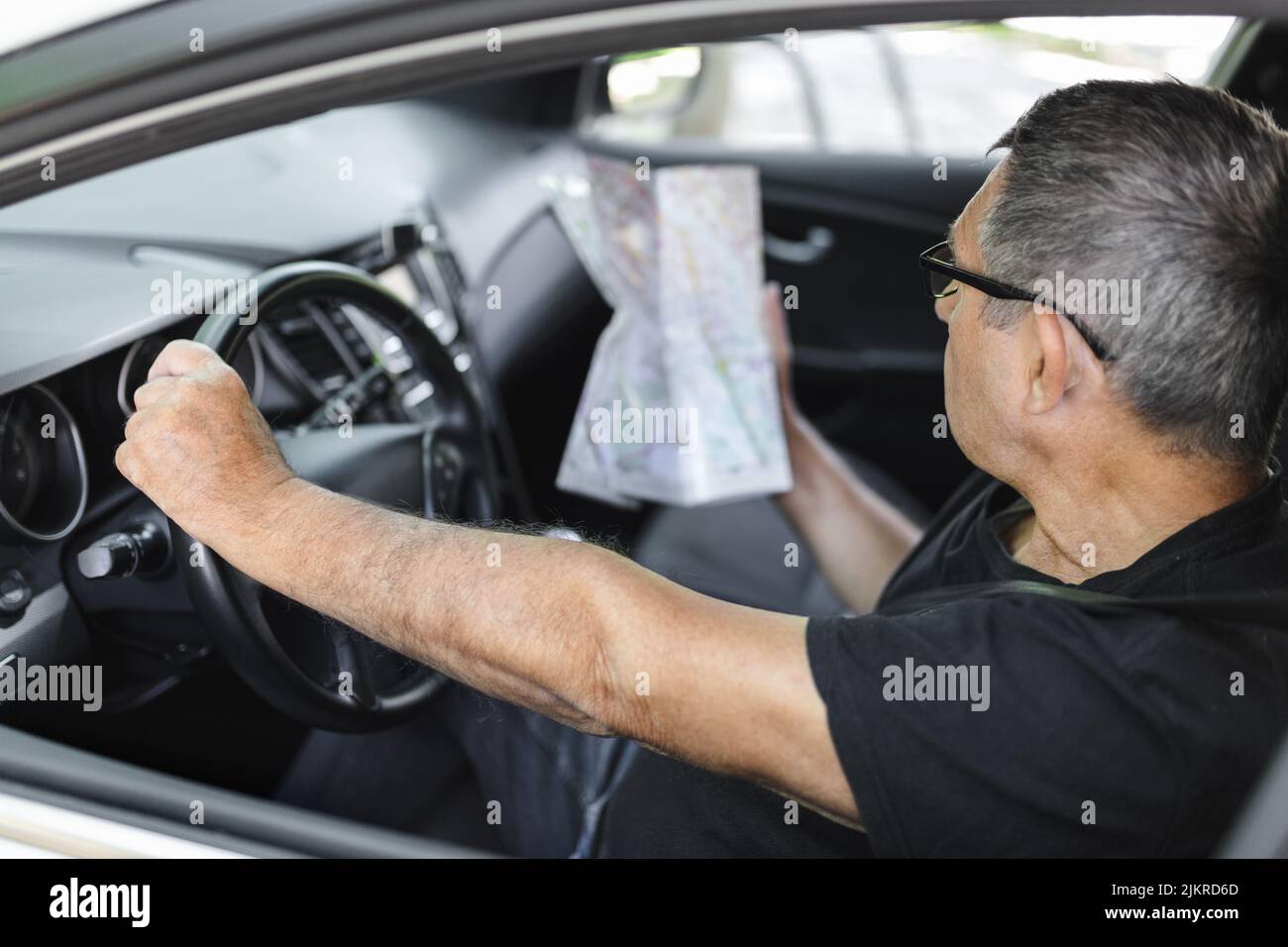 Senior behind the steering wheel of a car, looking at map for ...