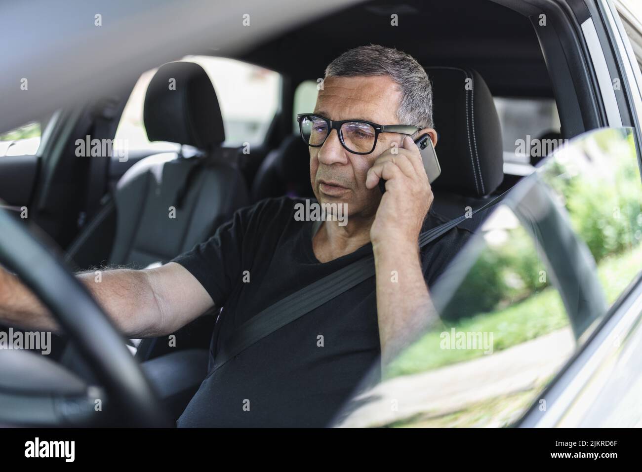 Active senior in his 70s driving a car and usig his mobile phone Stock ...