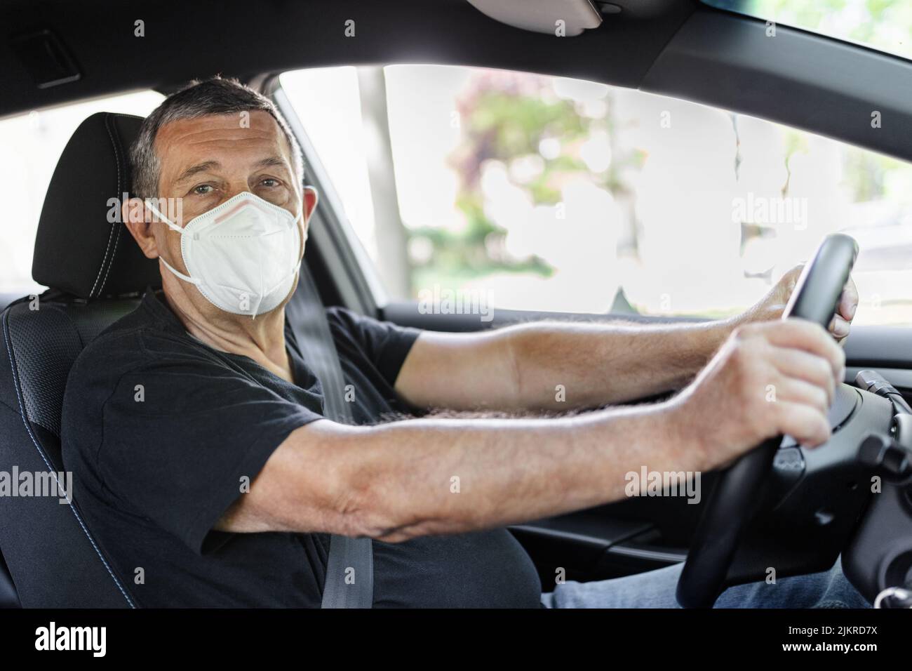 Senior in his 70s driving a car wearing face mask for protection ...