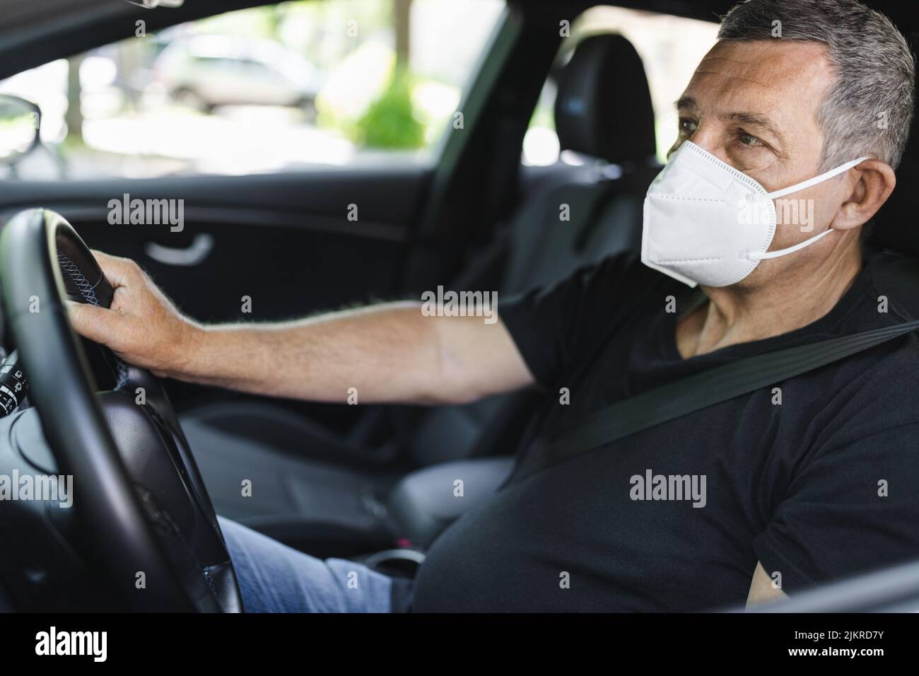 Senior in his 70s driving a car wearing face mask for protection ...