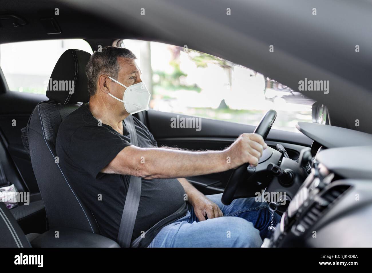 Senior in his 70s driving a car wearing face mask for protection ...