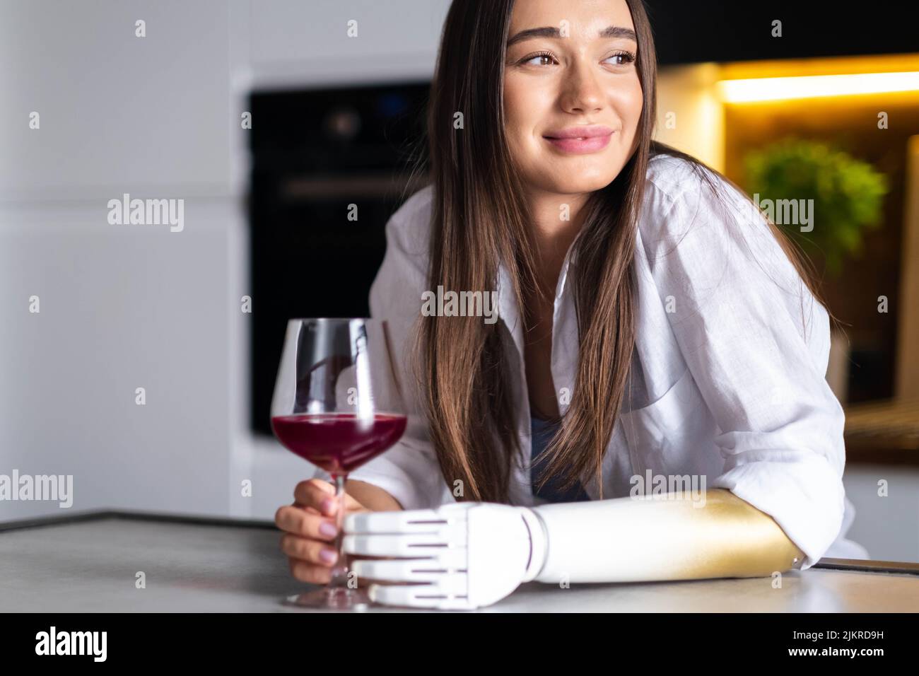 Happy girl with prosthetic arm holds glass of wine at home, woman with ...
