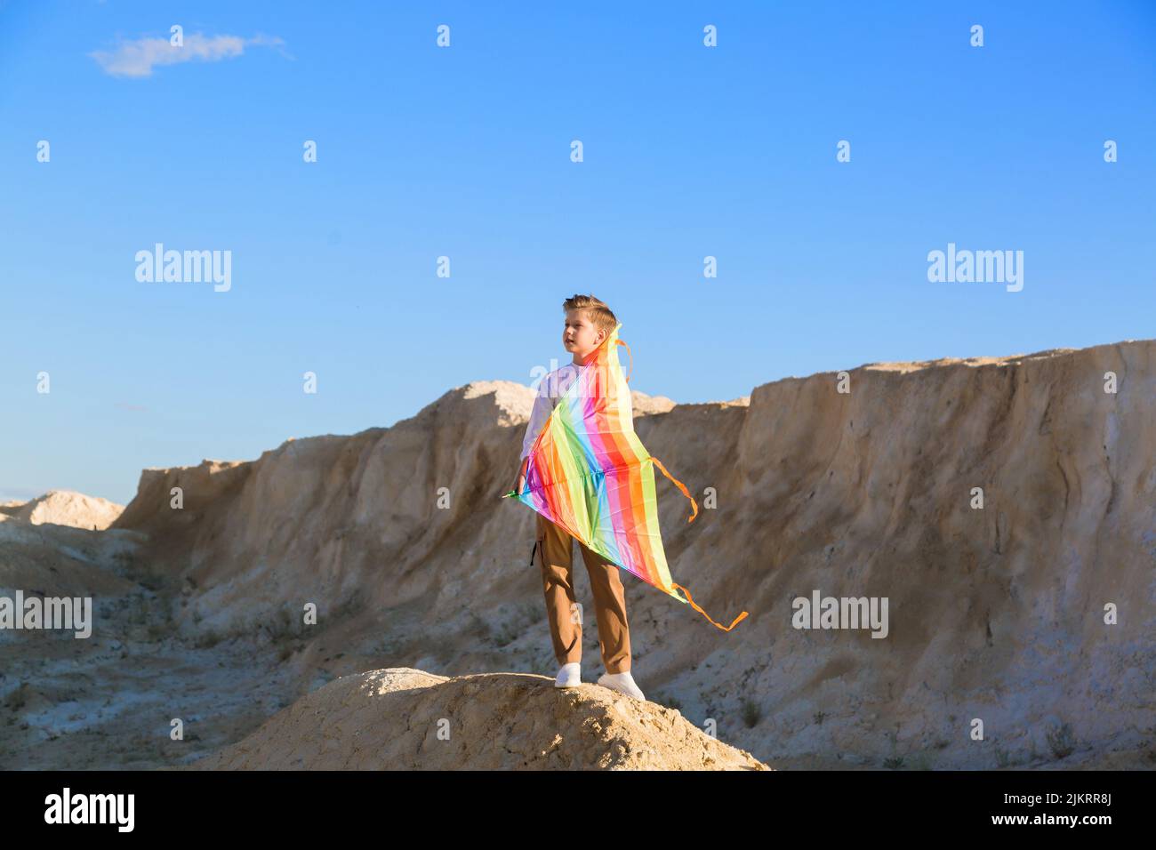 A boy with a kite stands on a mountain and looks into the distance. The ...