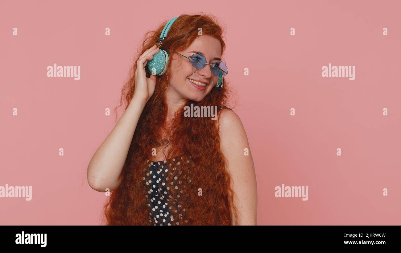 Young redhead woman in dress listening music on headphones, dancing ...