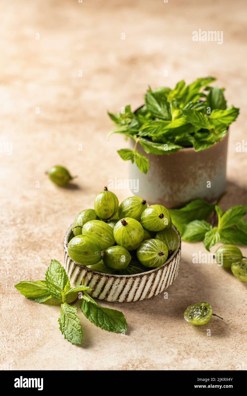 Ceramic bowl of raw healthy gooseberry with mint leaves on beige ...