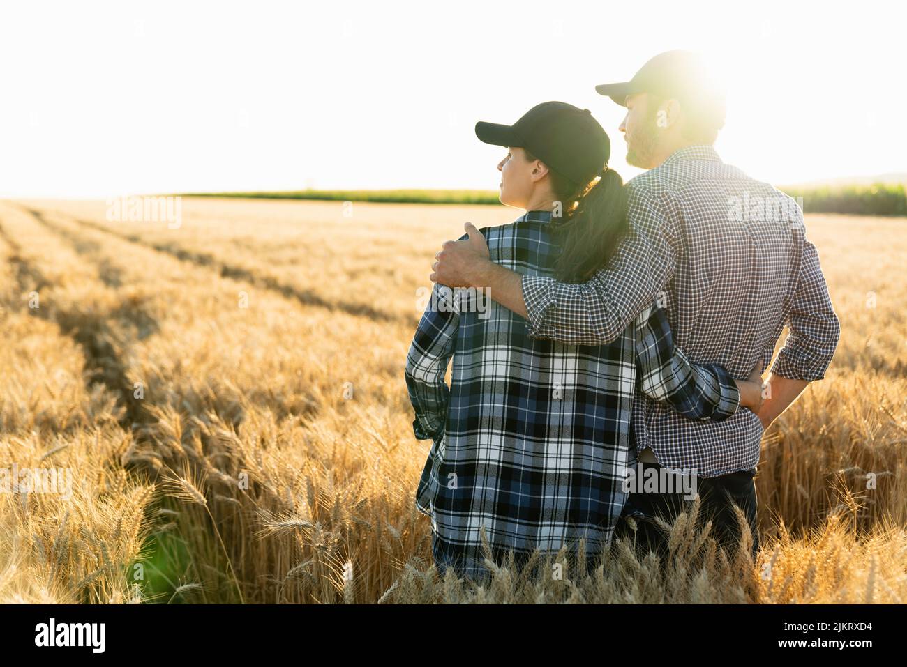 A couple of farmers in plaid shirts and caps stand embracing on ...