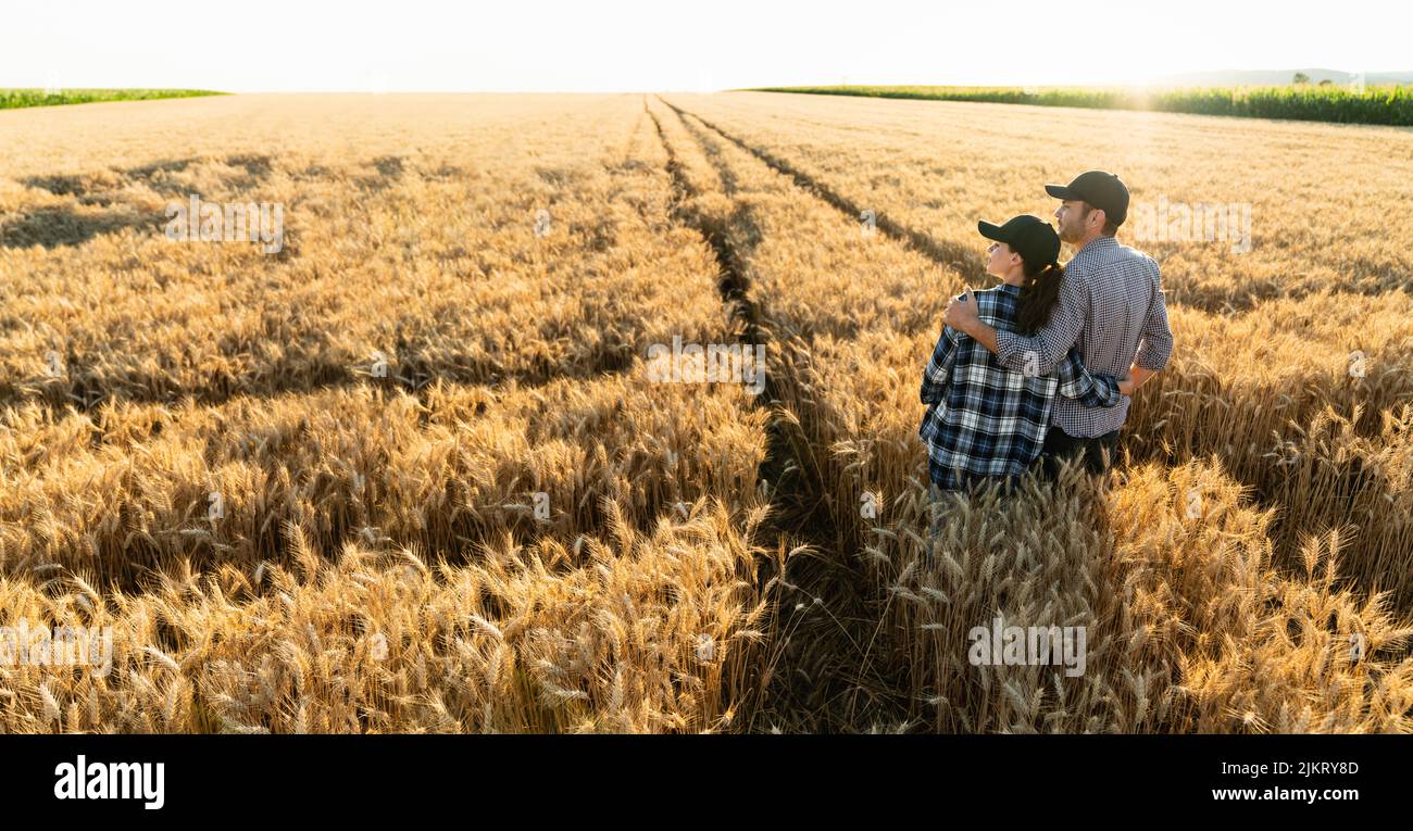 A couple of farmers in plaid shirts and caps stand embracing on ...