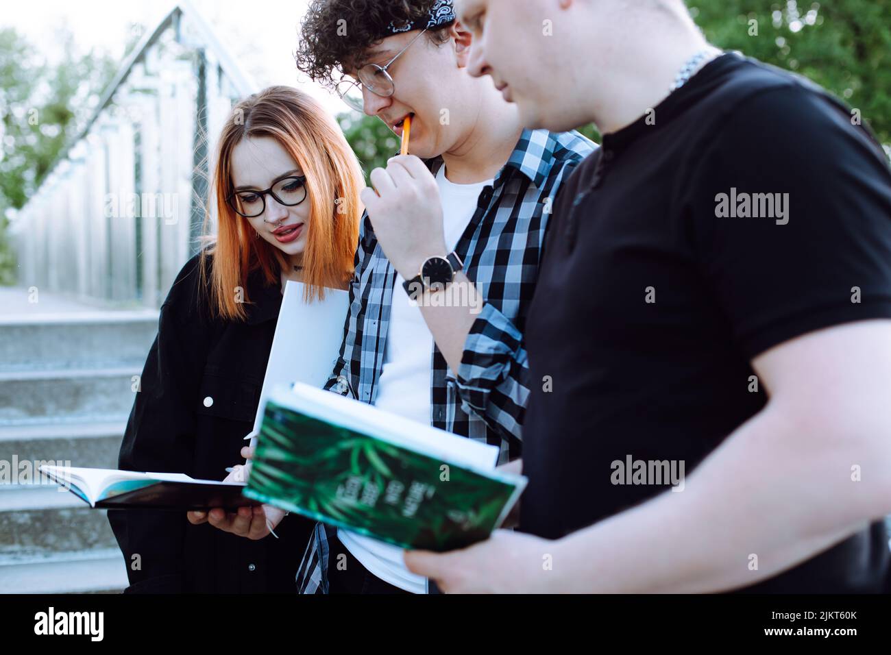 Three friends standing studying with book outdoors. Small group of high ...