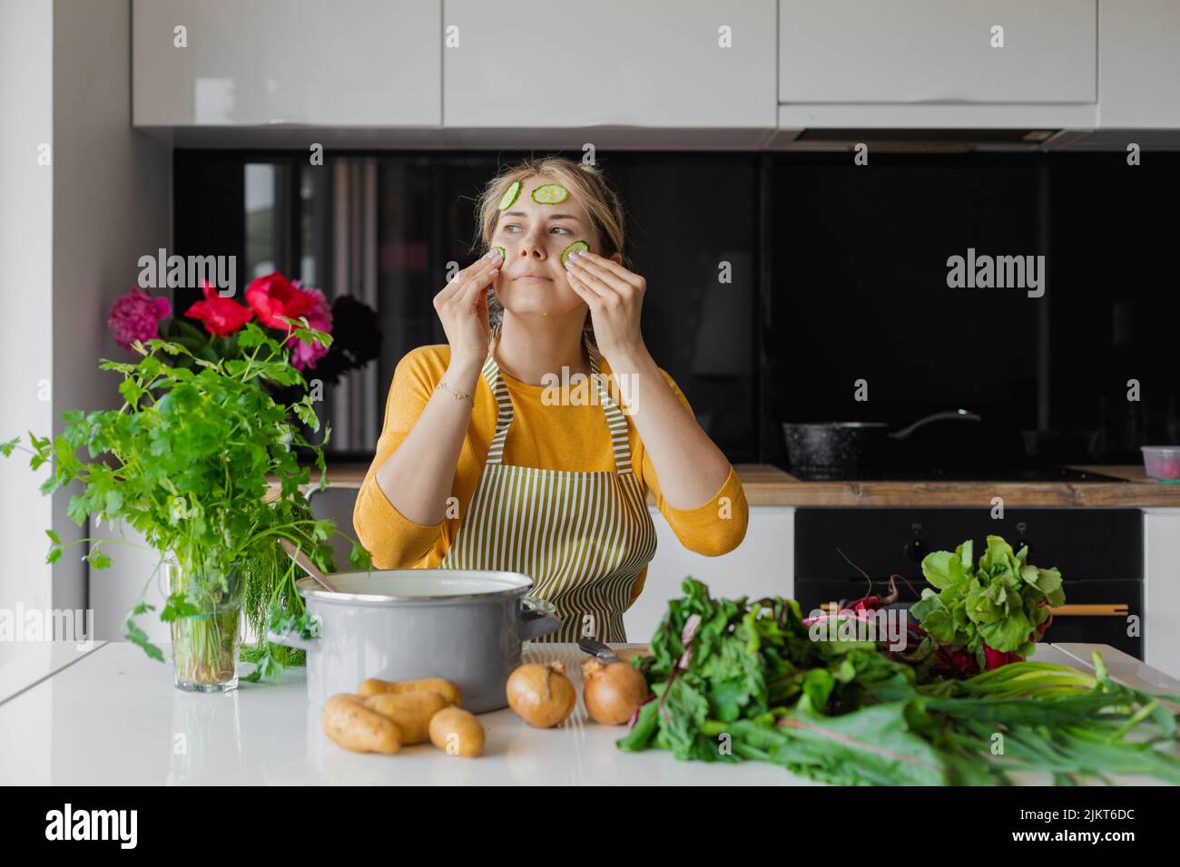 Funny blonde woman with cucumber slices on face, cook, eating in home ...