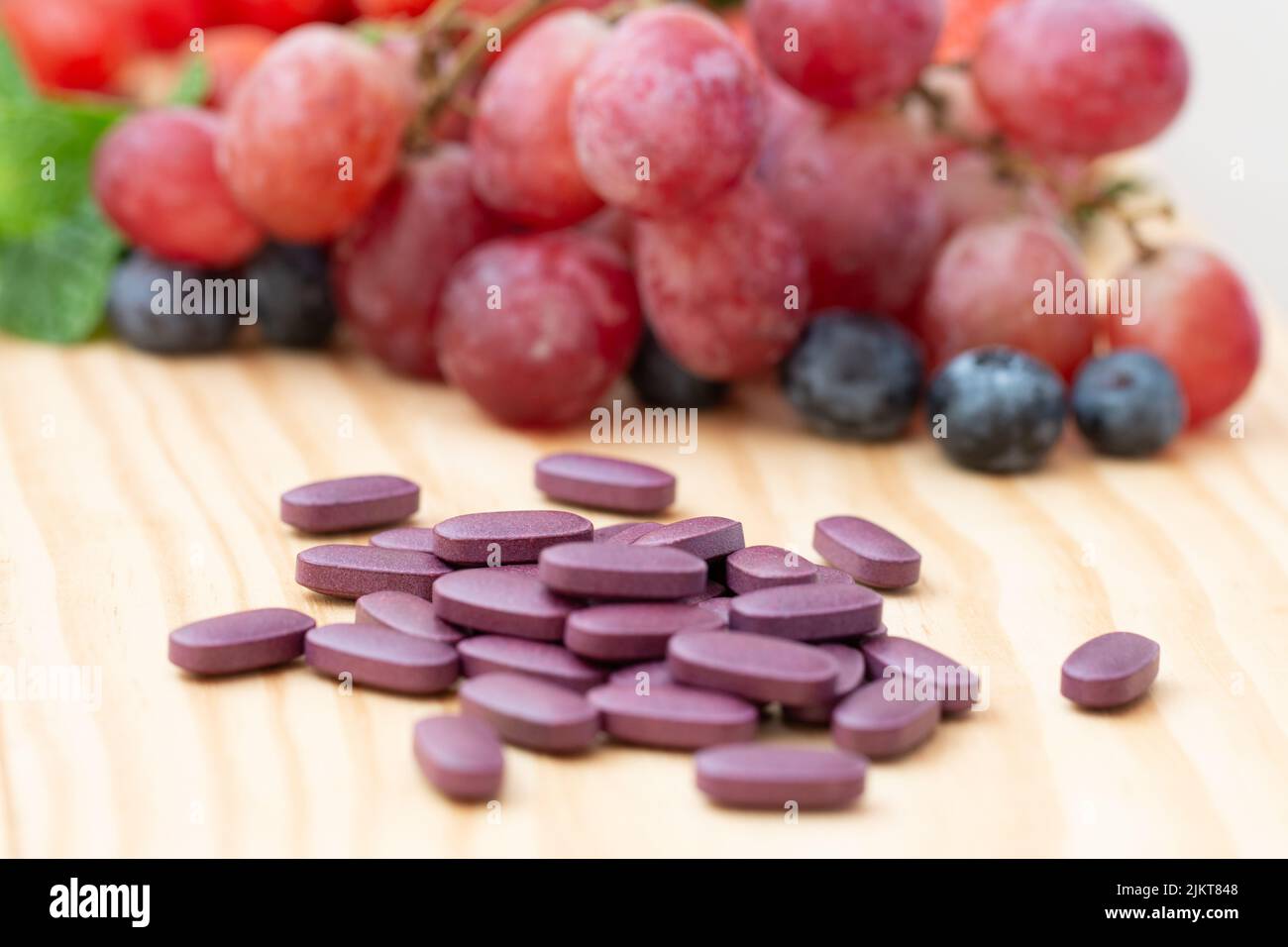 Purple vitamins supplements on the wooden table with variety fruit ...
