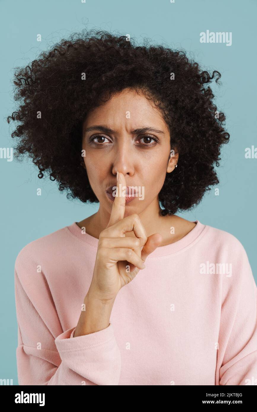 Black young woman frowning while silence gesture isolated over blue ...