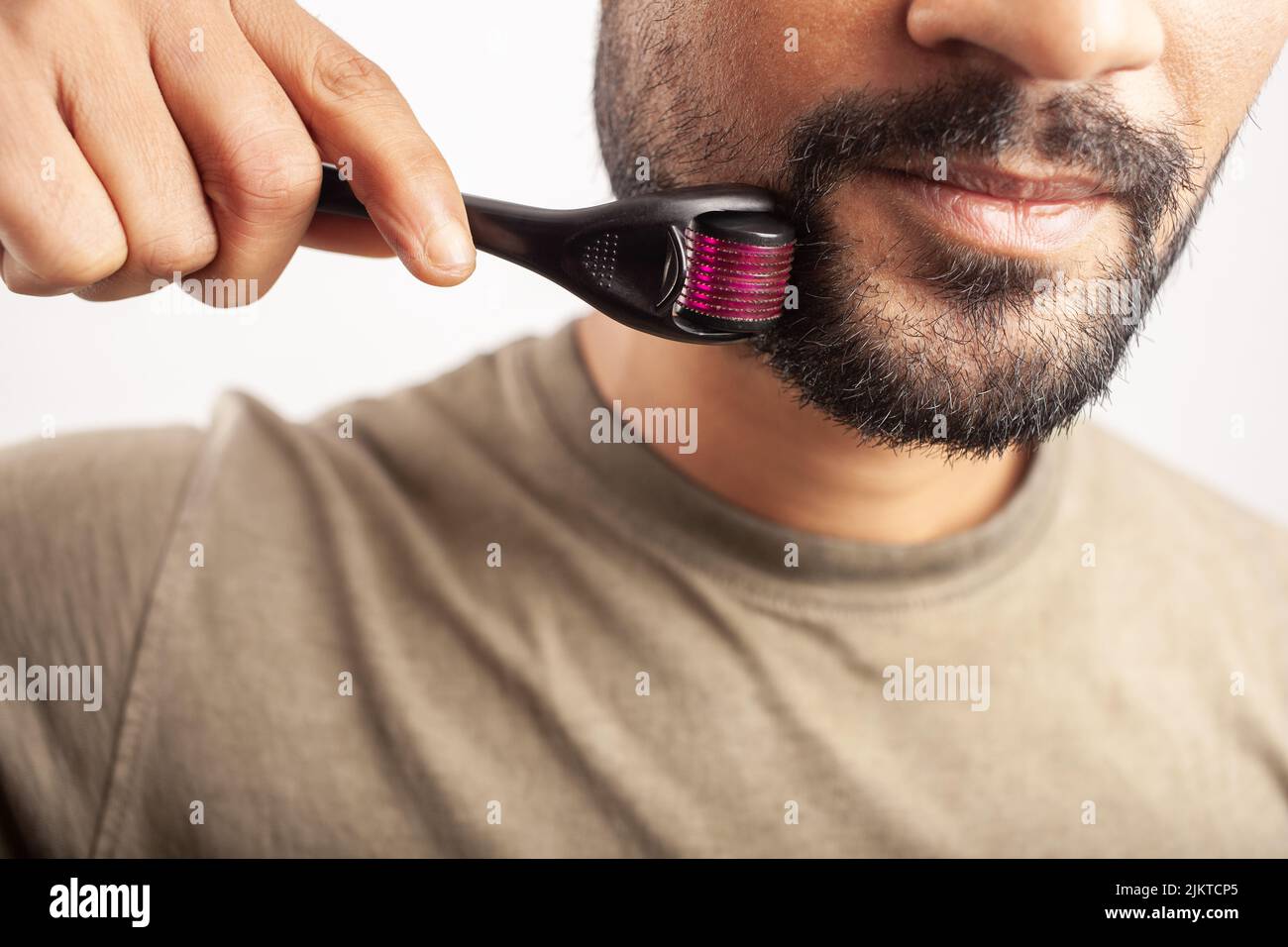 Indian guy in white background using microneedling for beard growth ...
