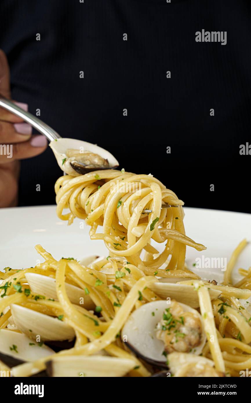 A vertical shot of a woman eating a delicious clam pasta Stock Photo ...