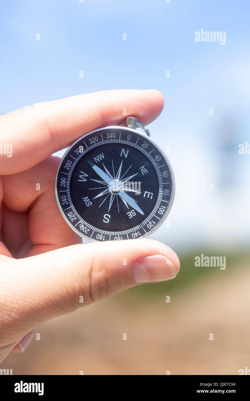 Closeup, hand holding an analog compass in front of a lighthouse on the ...