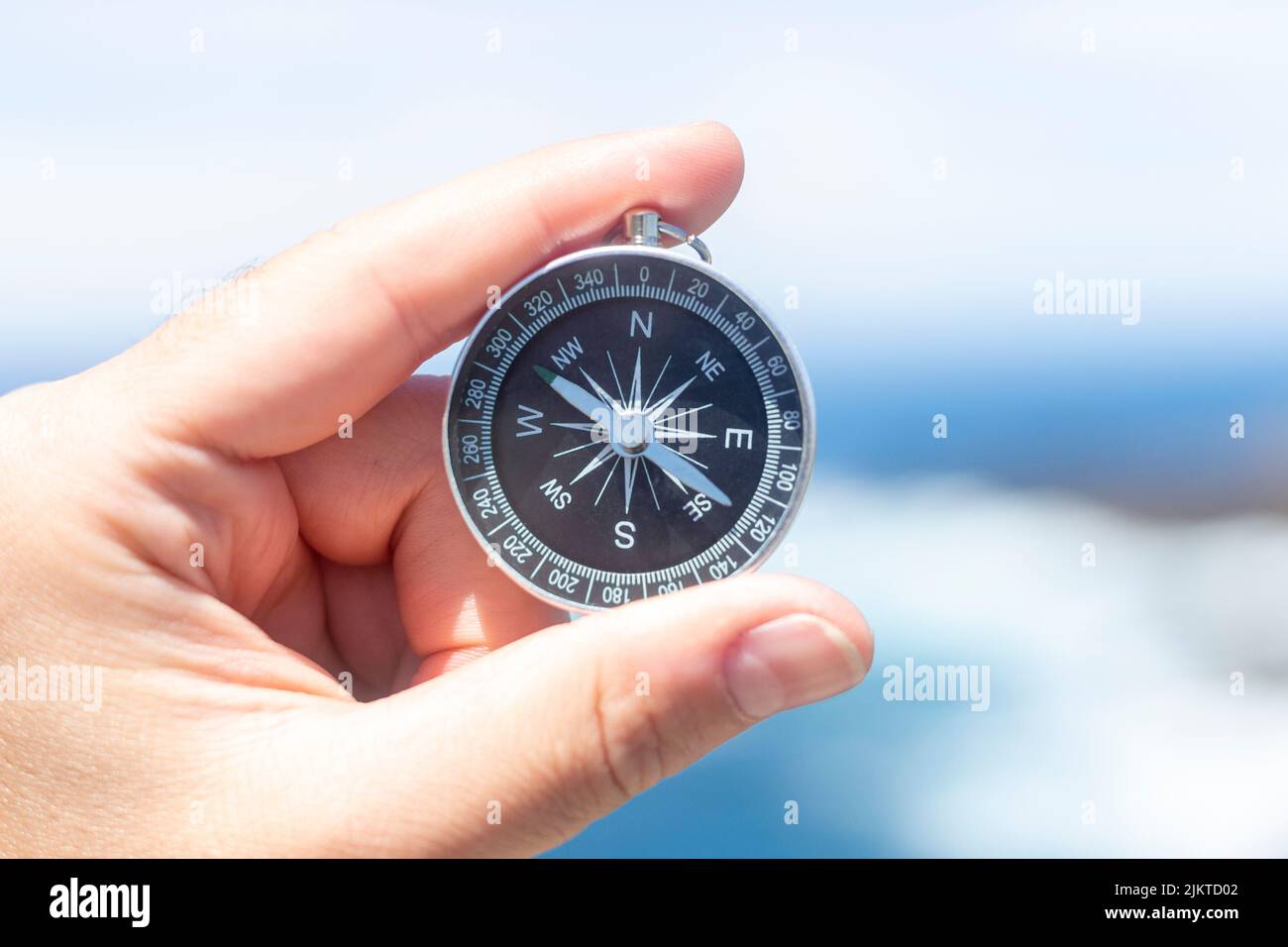 Closeup, hand holding an analog compass in front of the sea, summer ...