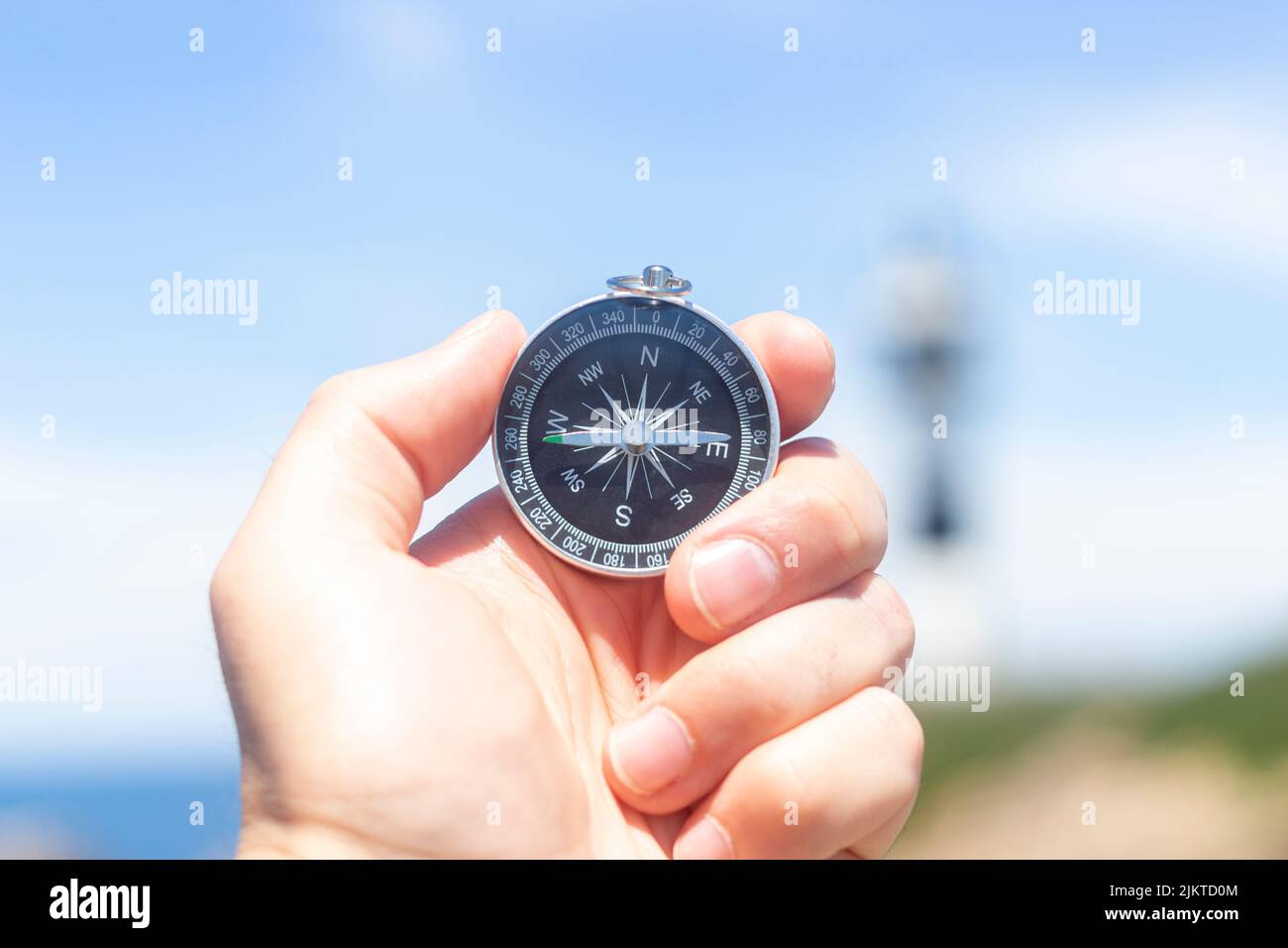 Closeup, hand holding an analog compass in front of a lighthouse on the ...