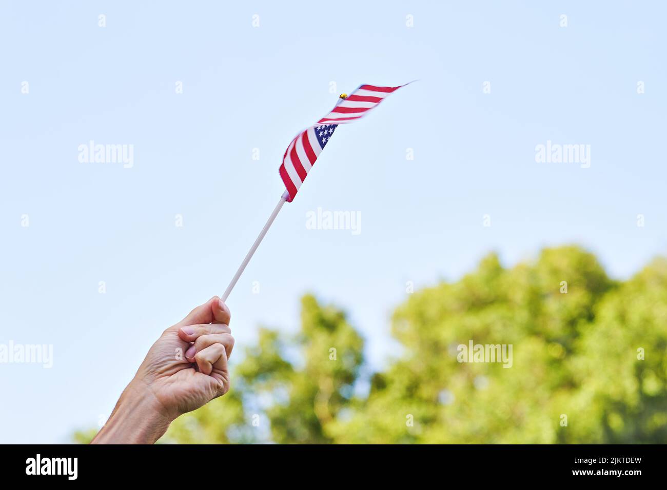Raised hand with waving American flag against blue sky. Celebration of ...