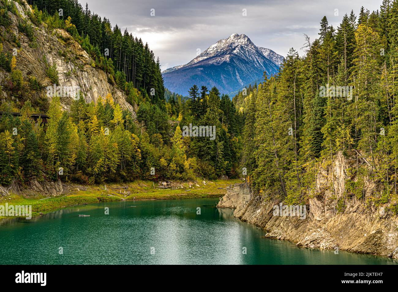 The green river surrounded by pine trees against the mountain peak ...