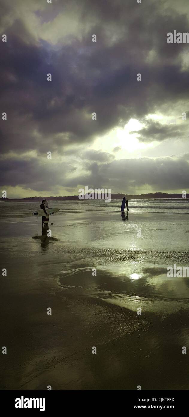 A vertical view of the sun shining behind dark clouds over the surfers ...