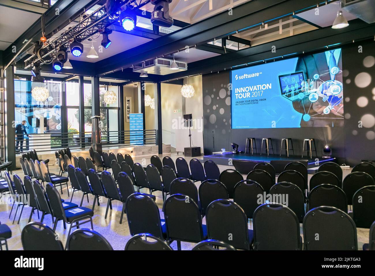 An Interior of a conference event venue with blue chairs and a screen ...