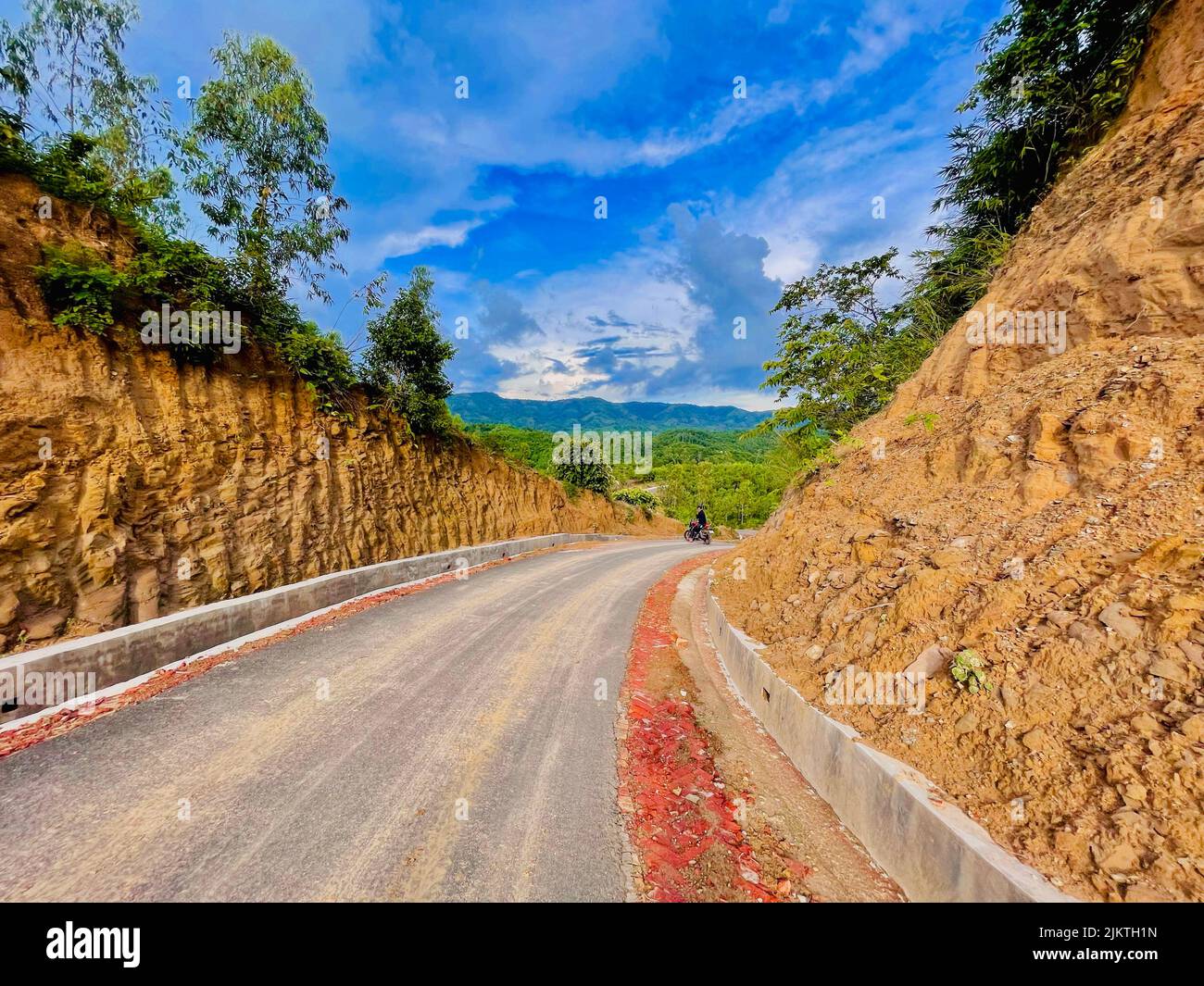 A curving road between two steep hills with lush greenery around it ...