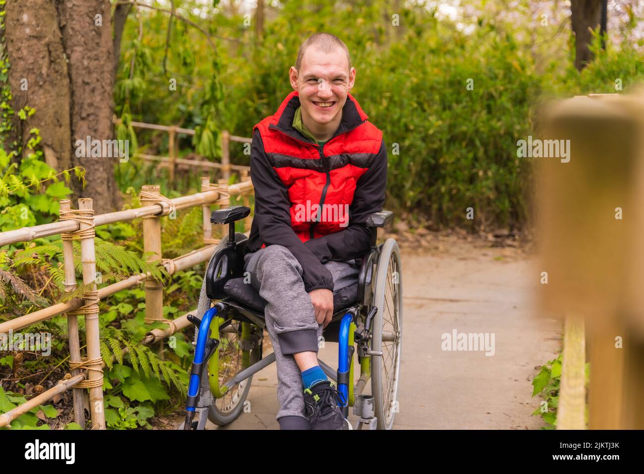 Portrait of a paralyzed young man in a public park in the city. Sitting ...