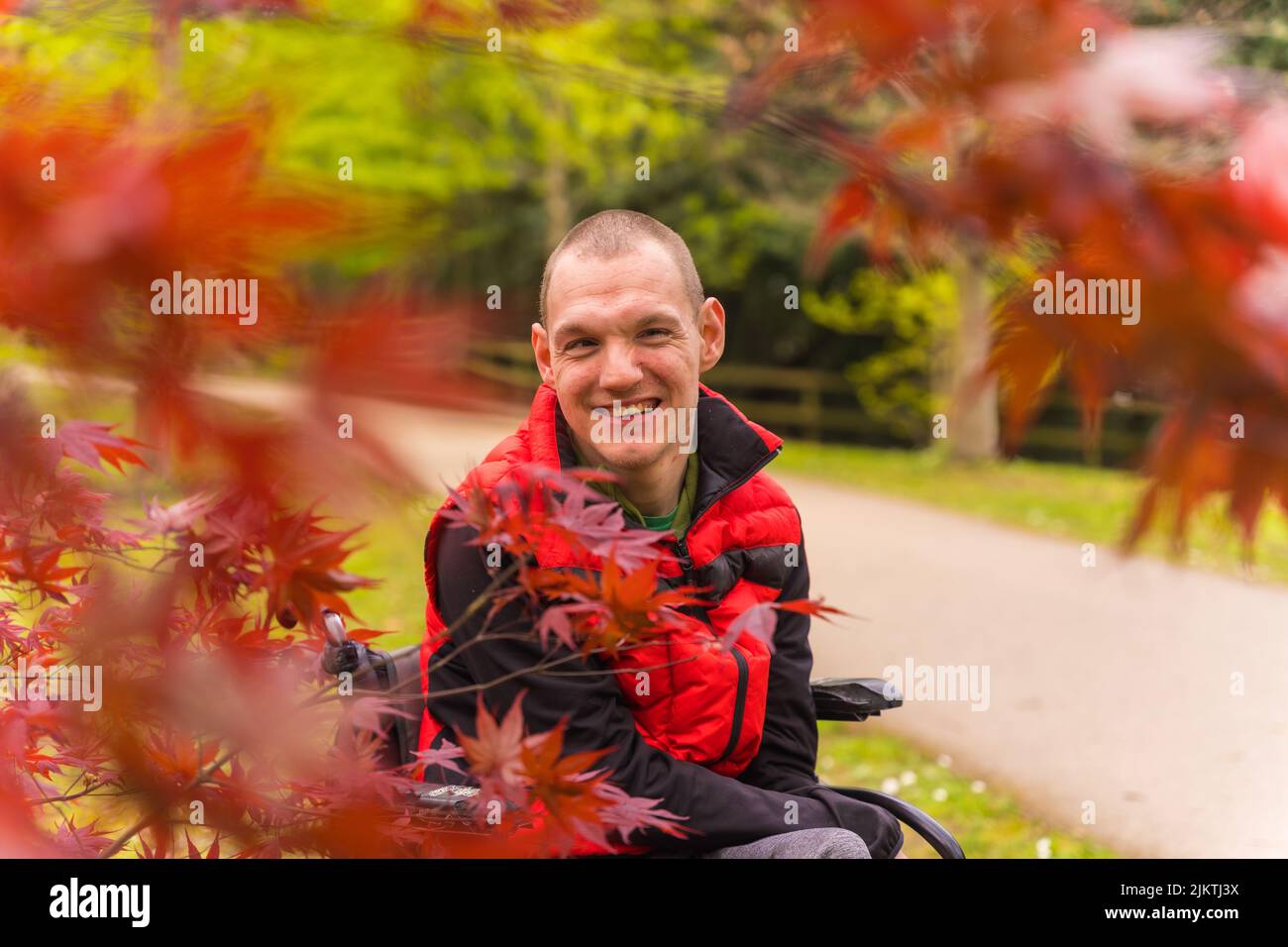 Portrait of a paralyzed young man in a red vest in a public park in the ...